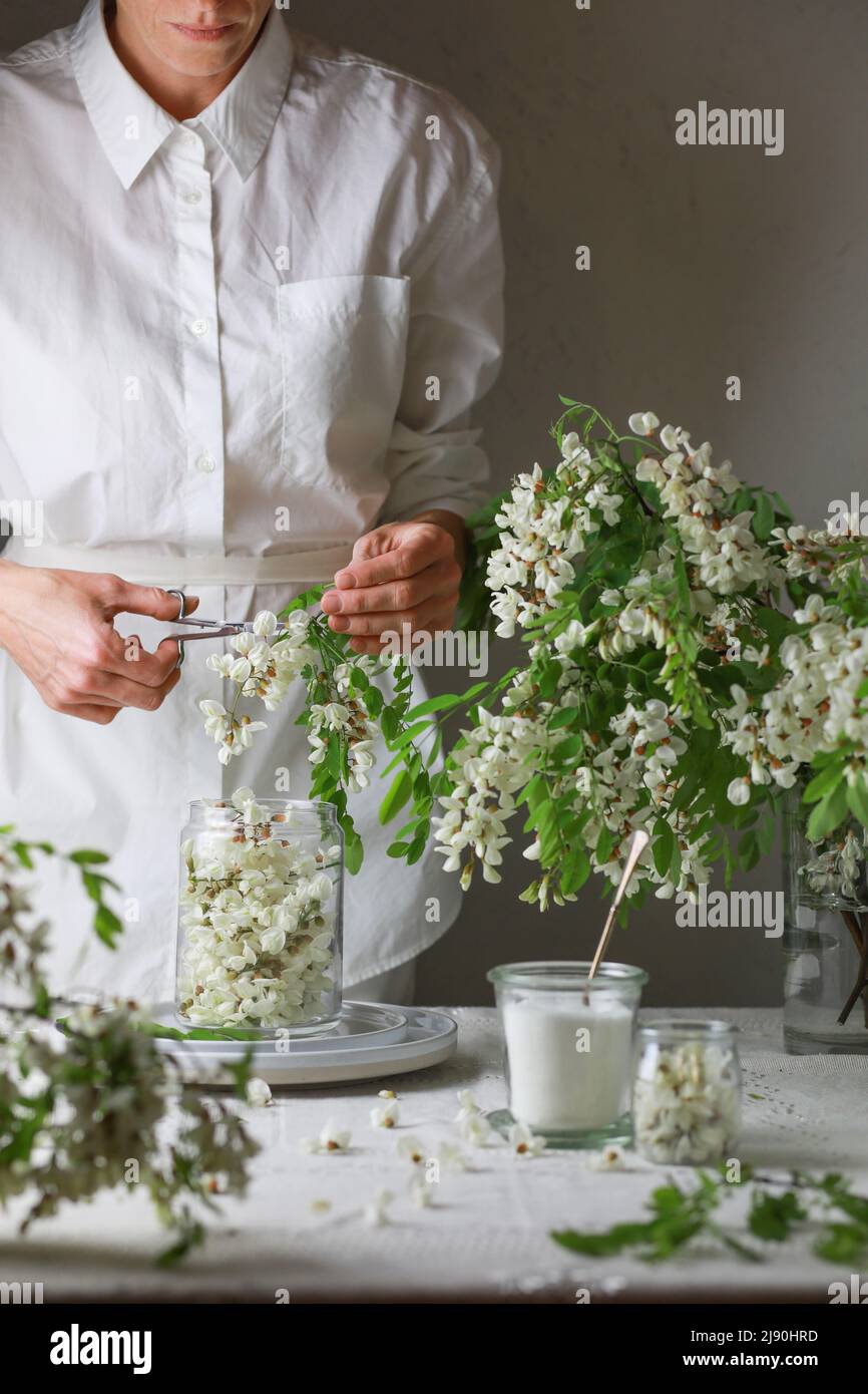 Woman wearing in white dress put acacia flowers in a jar. Girl prepares ...