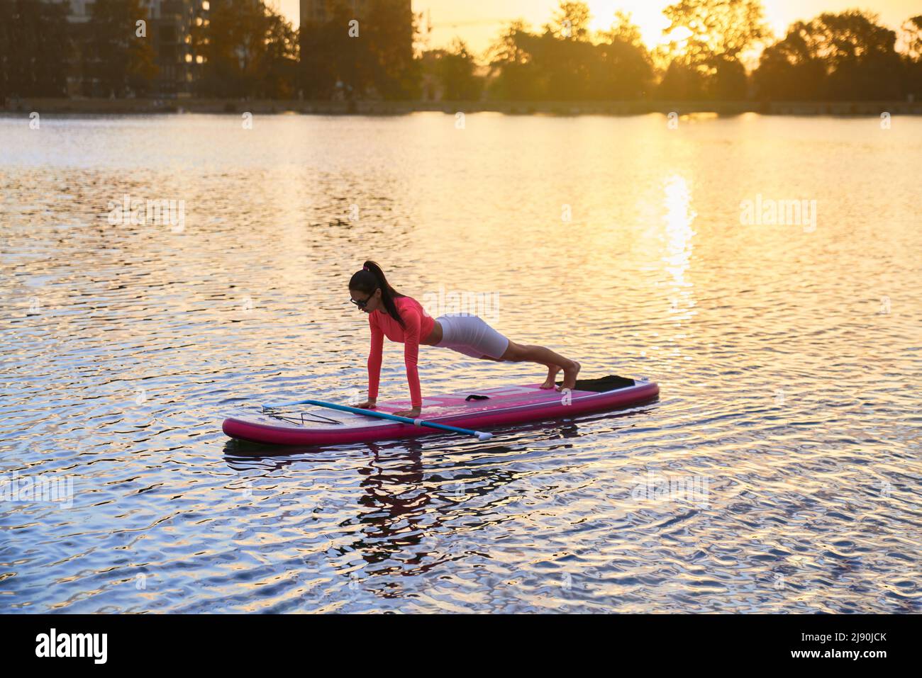 Sporty caucasian woman doing plank exercises while floating on paddle ...