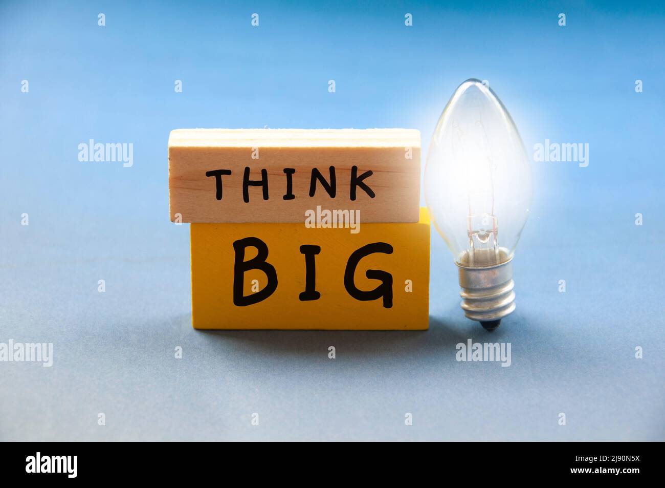 Think big text on wooden blocks with shining bulb on light blue ...
