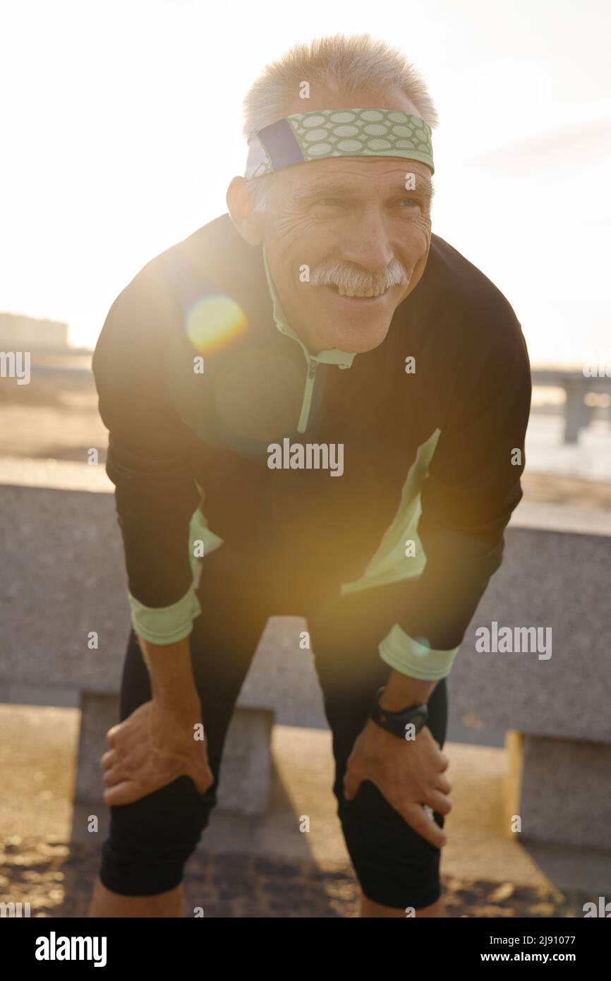 Aged man in sportswear bending forward smiling looking away vertical ...
