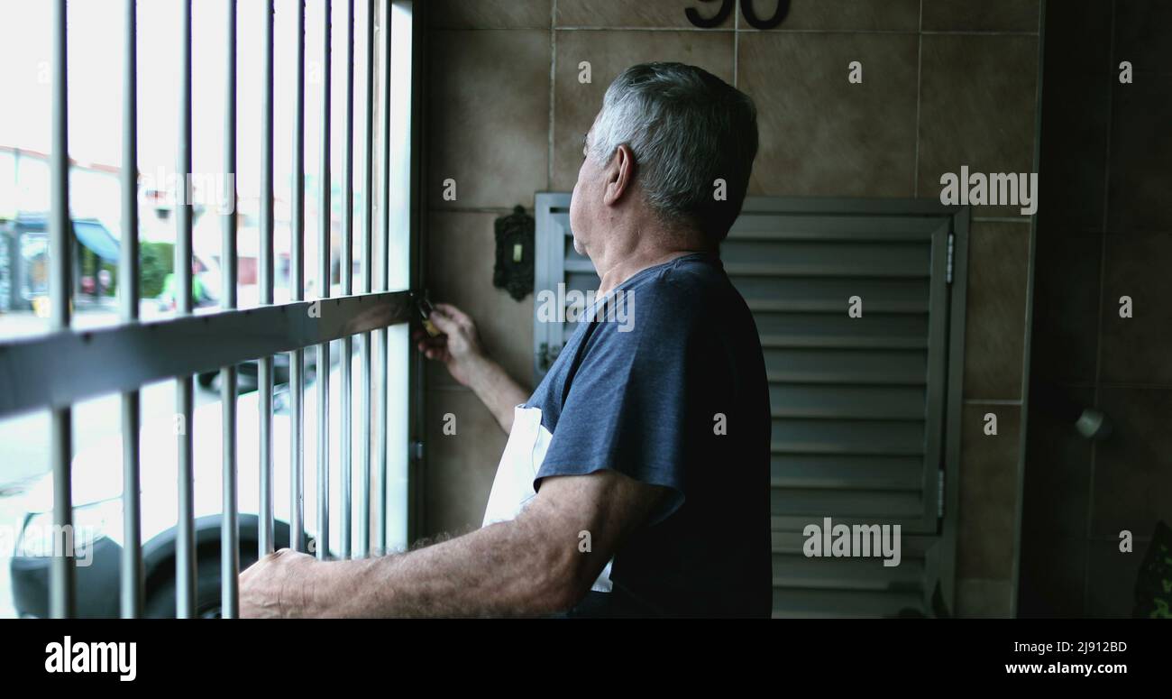 Old man arriving home, sliding metal garage gate. Senior entering house ...