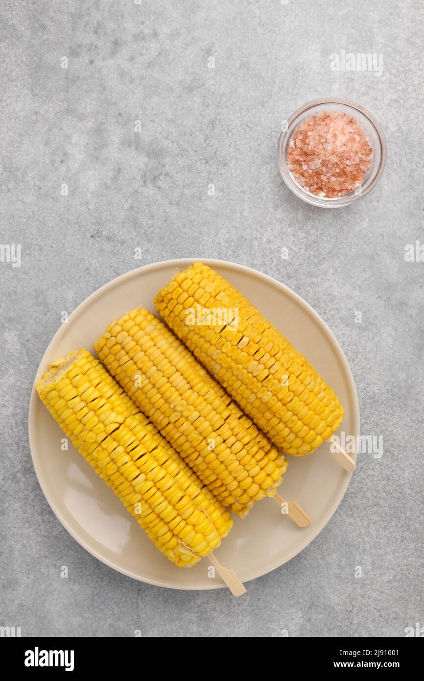 Boiled corn cobs on plate and bowl of Himalayan salt, gray background ...