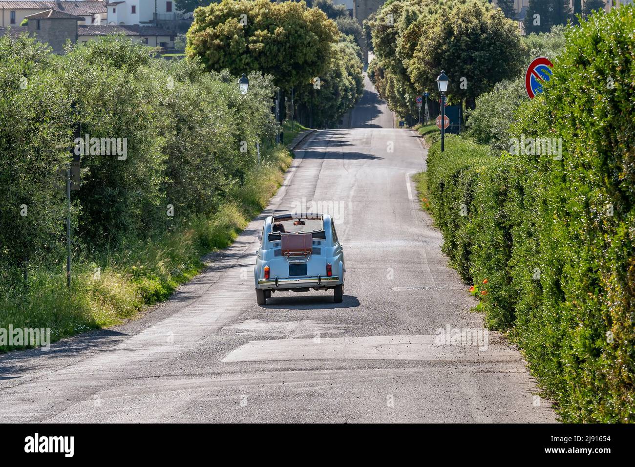 A vintage Italian convertible car drives along a typical Tuscan tree ...