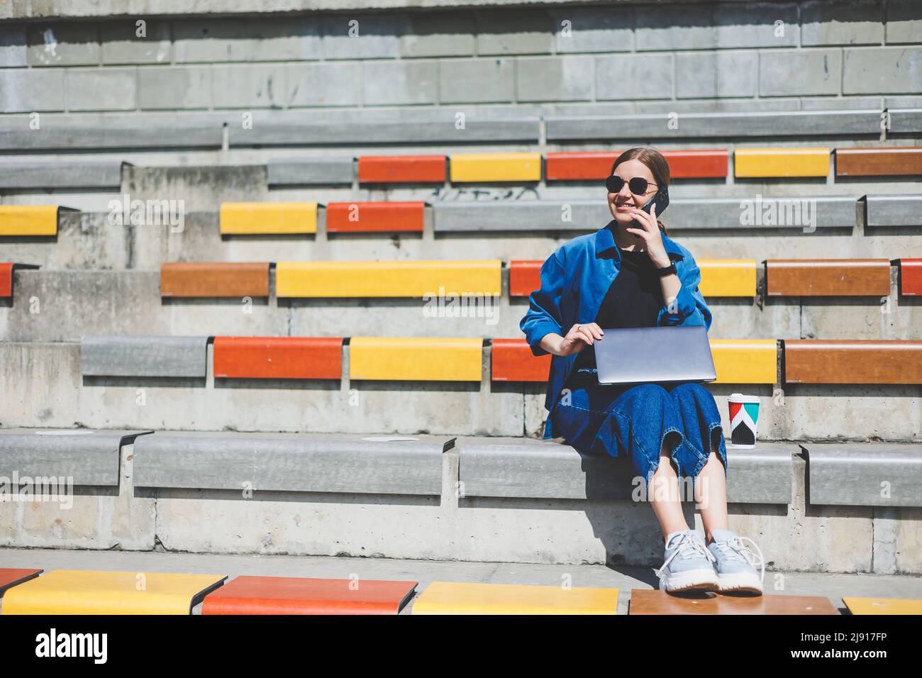 young pretty woman sitting with laptop in modern park street using ...