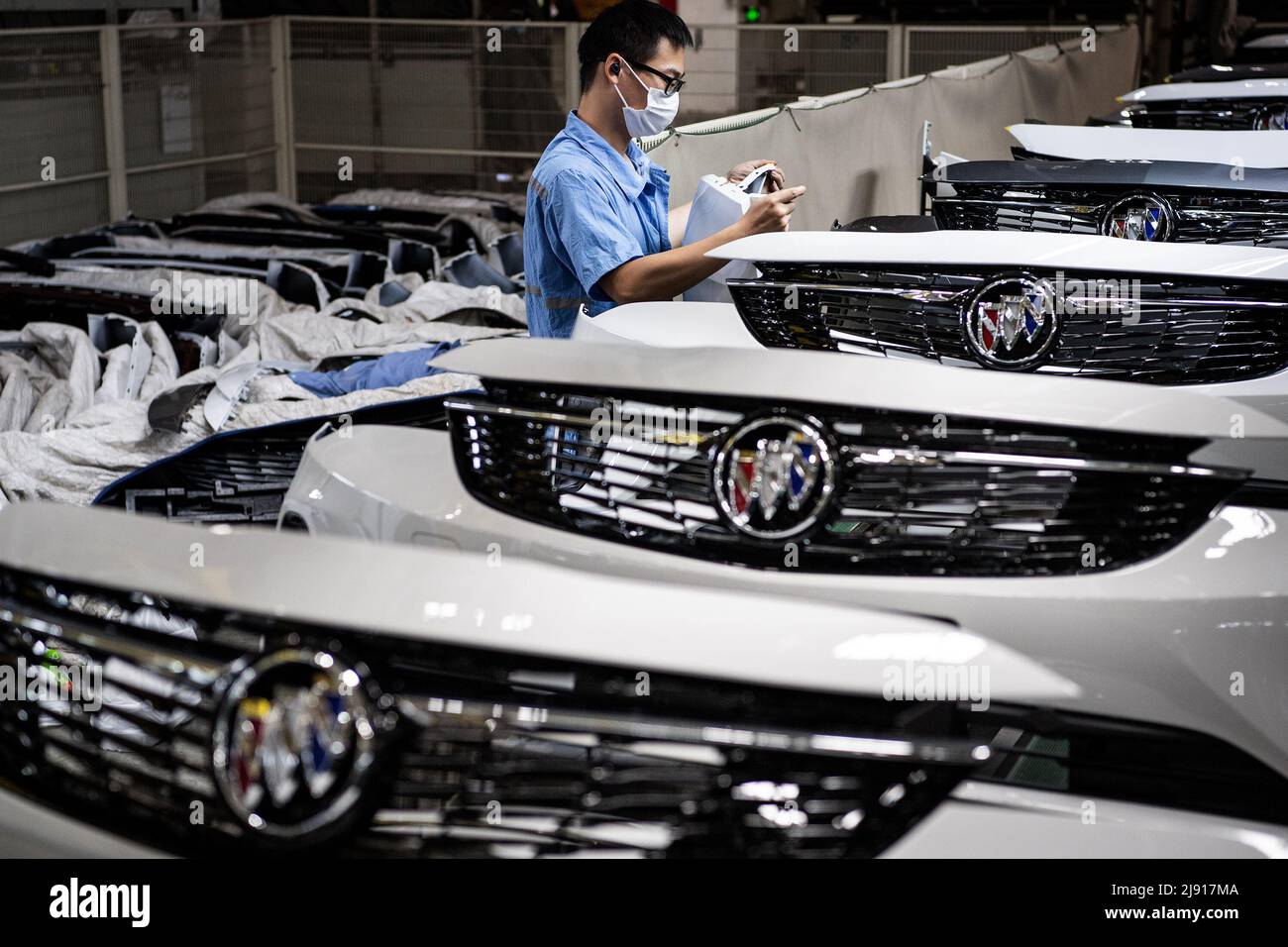 An employee wearing a mask works on a car assembly line at the SAIC ...