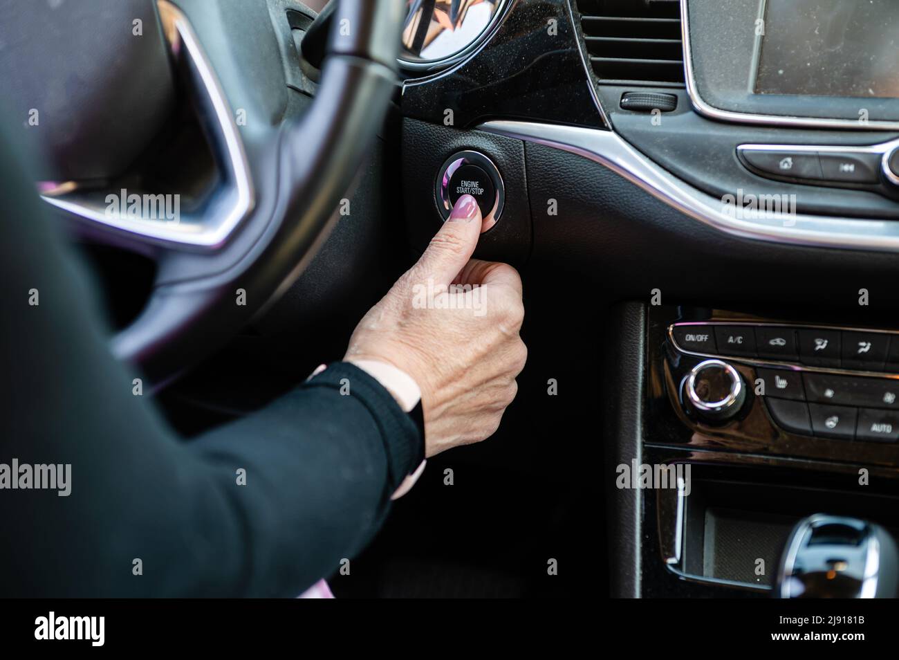 Woman starts the car engine with start-stop button. Modern car interior ...