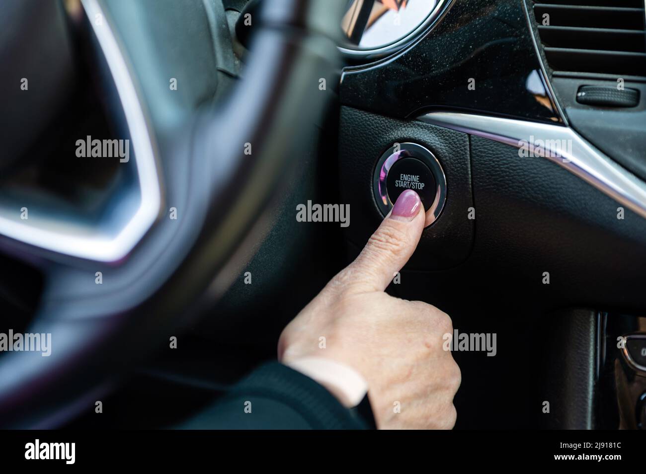 Woman starts the car engine with start-stop button. Modern car interior ...