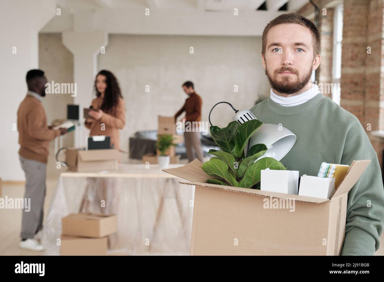 Portrait of serious young bearded company employee in sweater holding ...