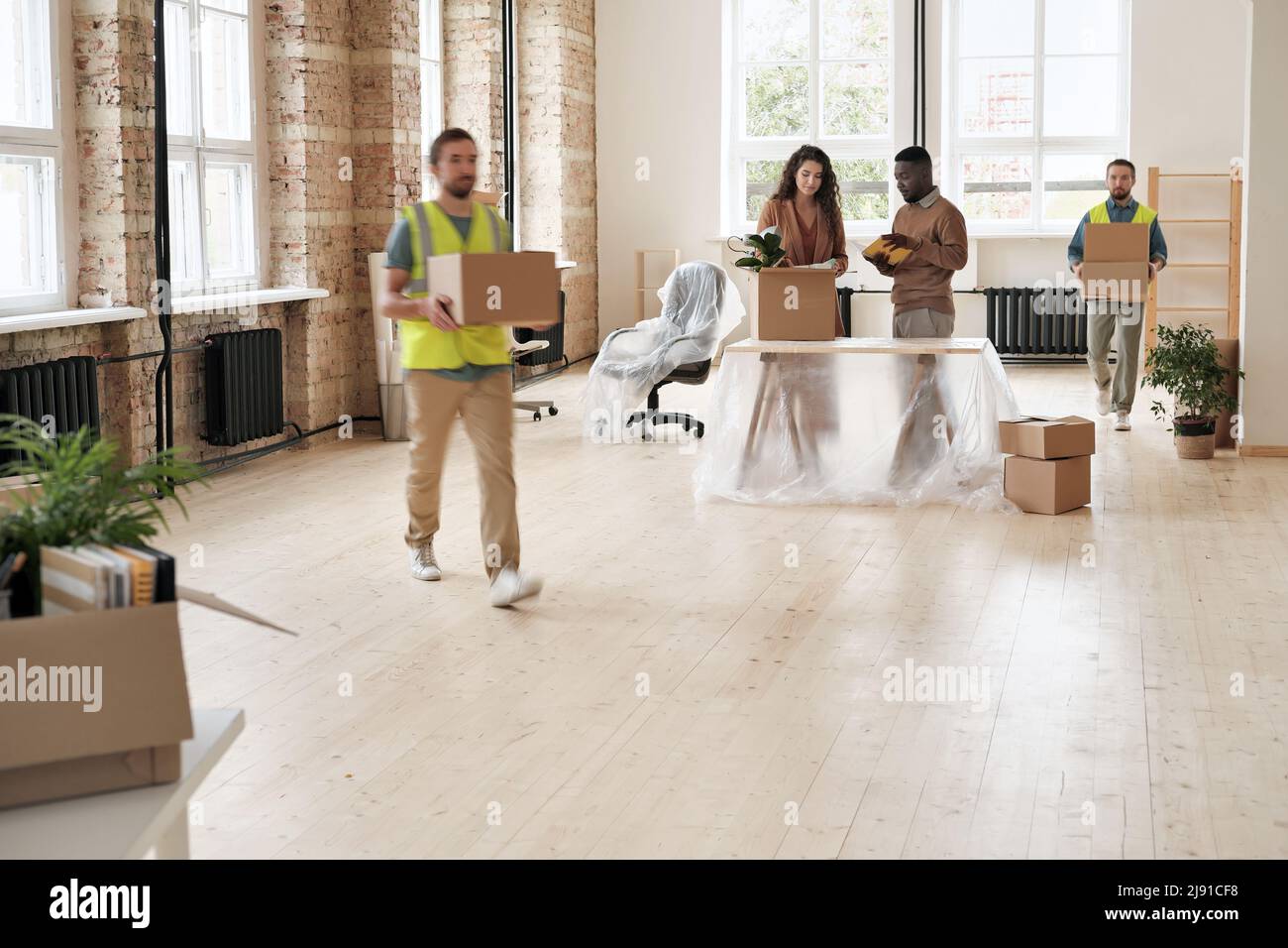 Loaders in vests carrying moving boxes in office while multi-ethnic ...
