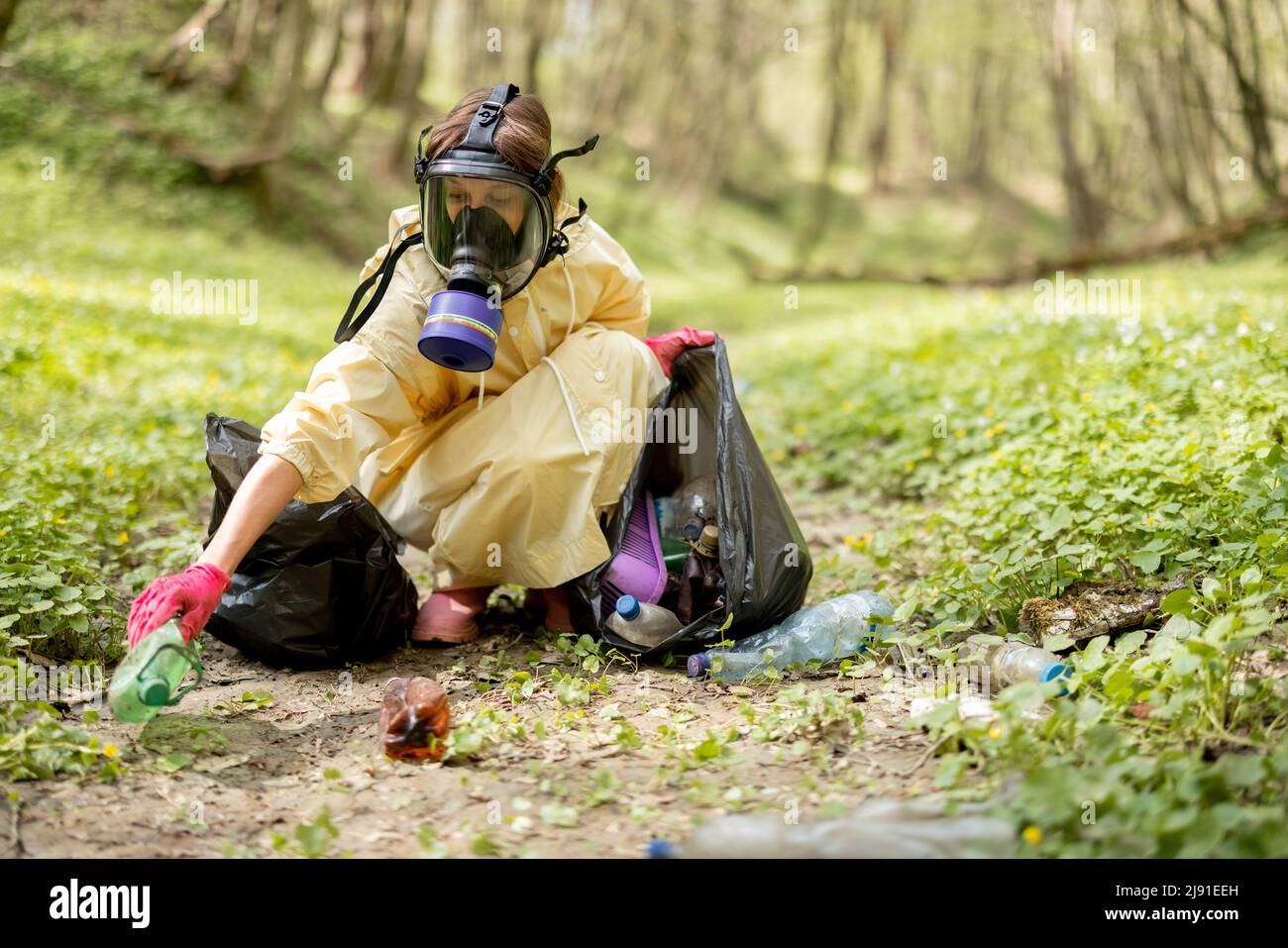 Woman in gas mask and protective clothes collecting scattered plastic ...