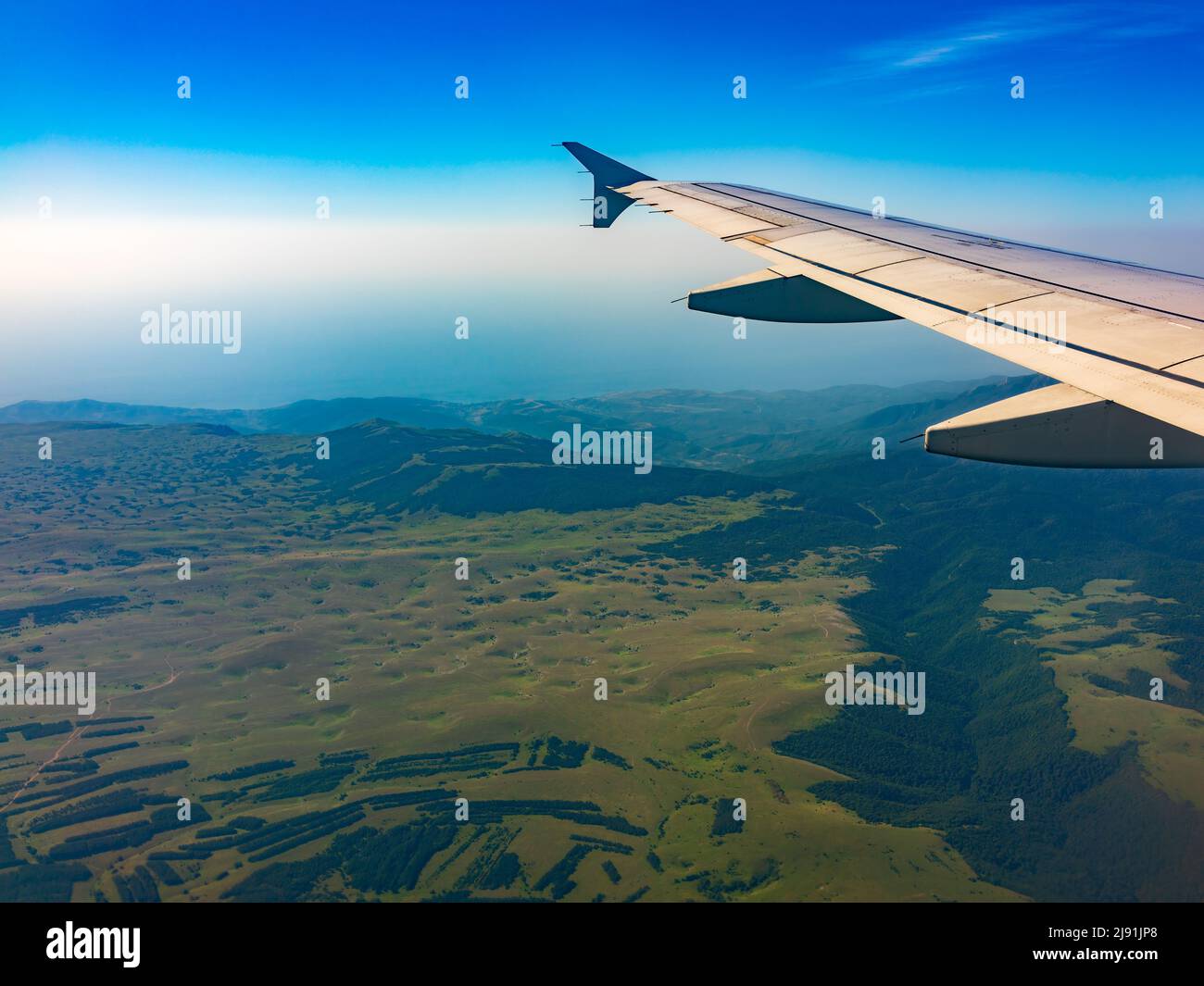 View of airplane wing, blue skies and green land during landing ...