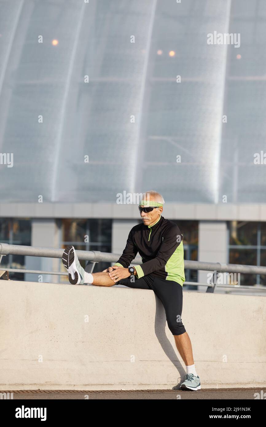 Vertical shot of slim elderly man doing ligaments stretching exercise ...