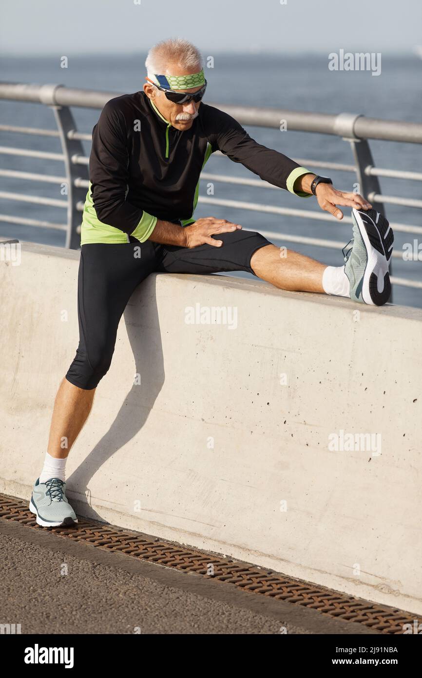 Modern senior man wearing tracksuit doing stretching exercises standing ...