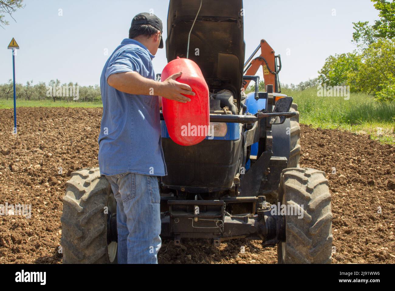Image of a farmer who with a jerrycan puts diesel fuel to the tractor ...