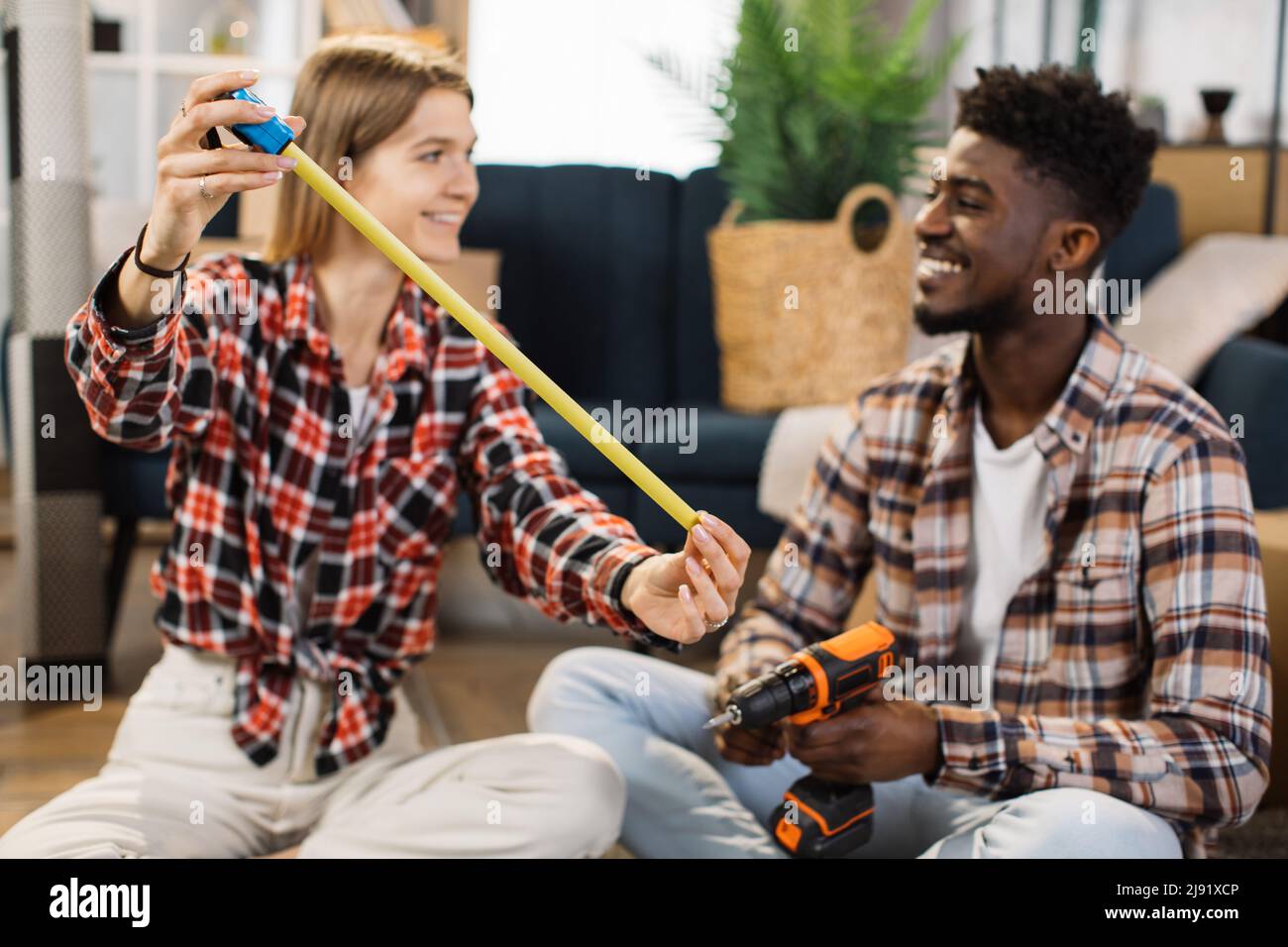 Young woman with measure tape looking at smiling man with electric ...