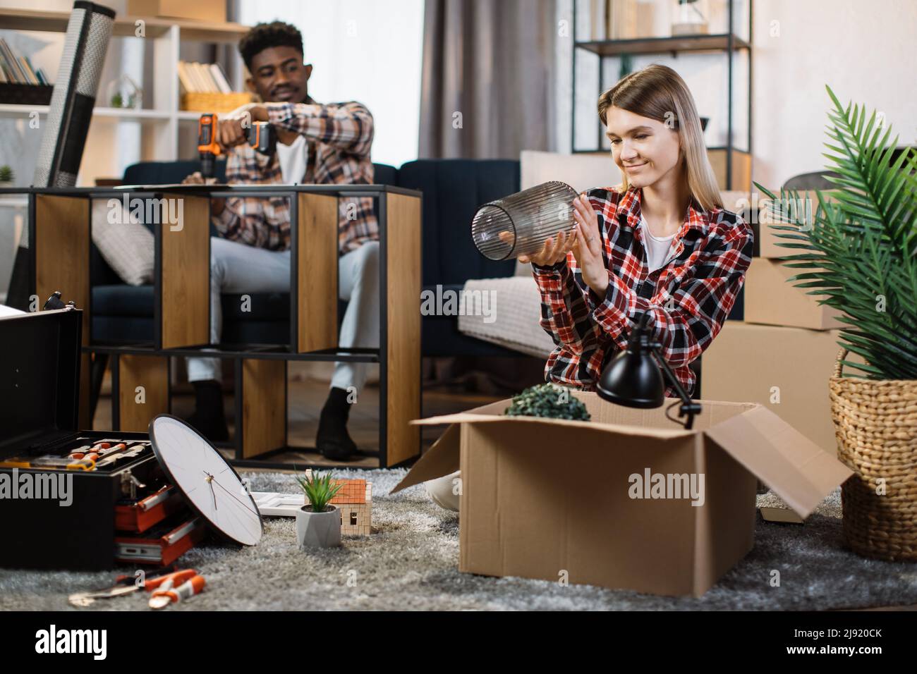 Young caucasian woman taking objects out of cardboard boxes while ...