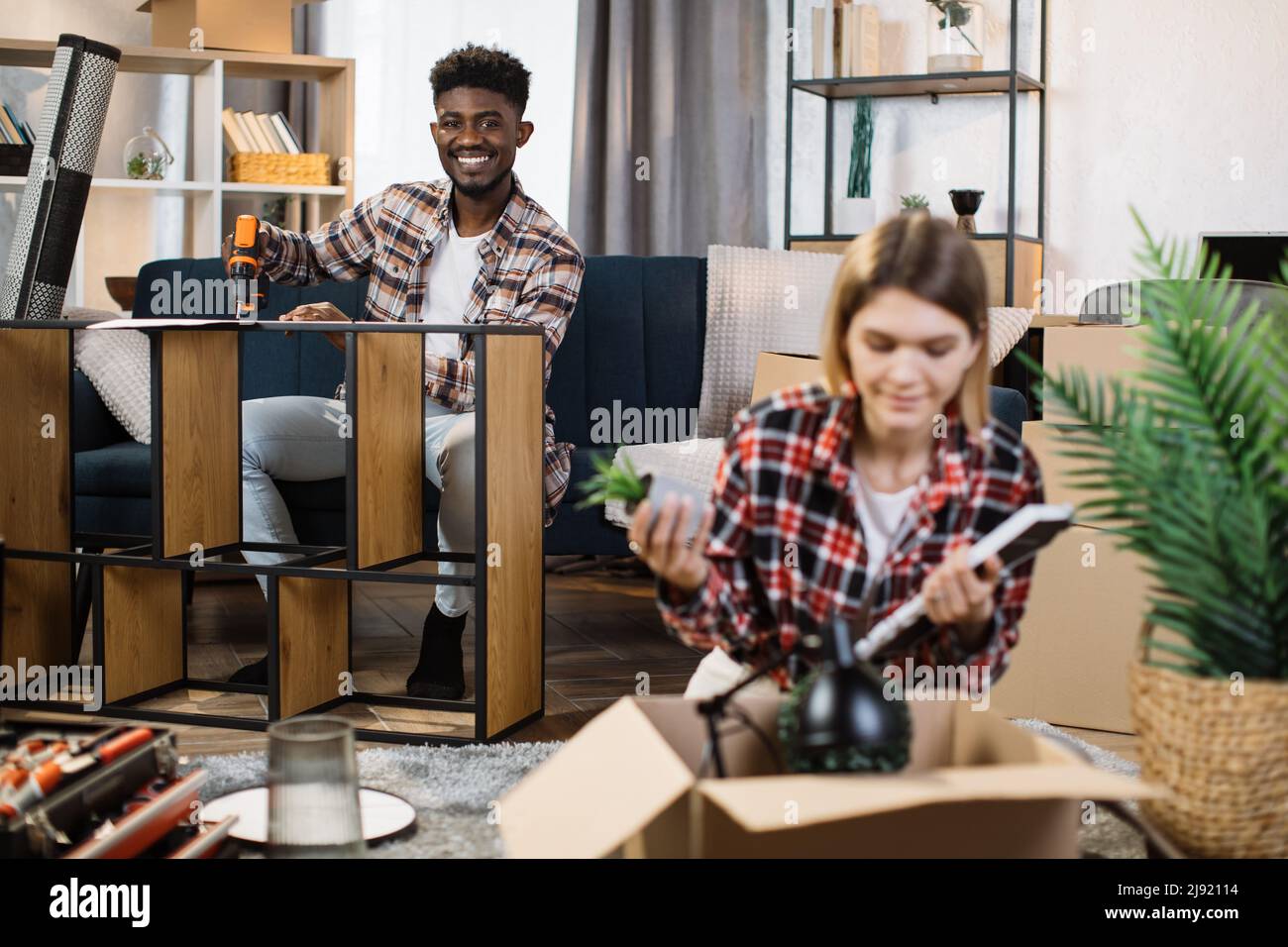 African american man using hand drill for assembling wooden shelves ...