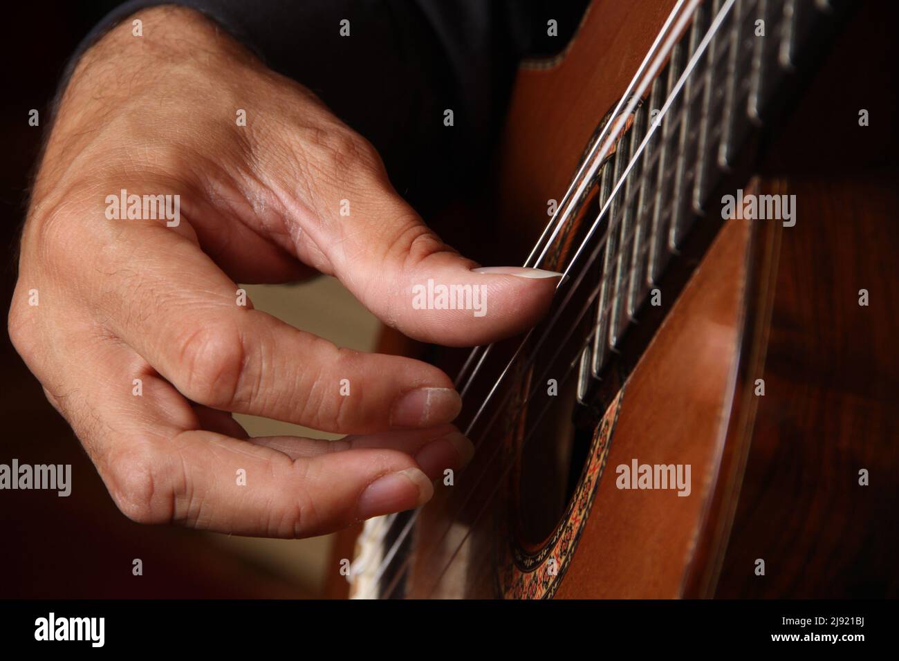 Male guitarist hands playing the strings of an acoustic guitar in ...