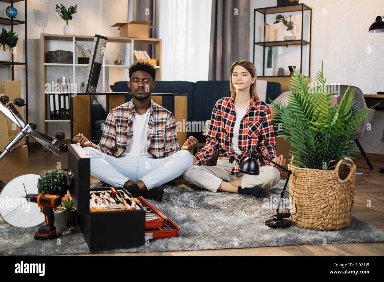 Relaxed multi ethnic couple sitting in lotus position and meditating on ...