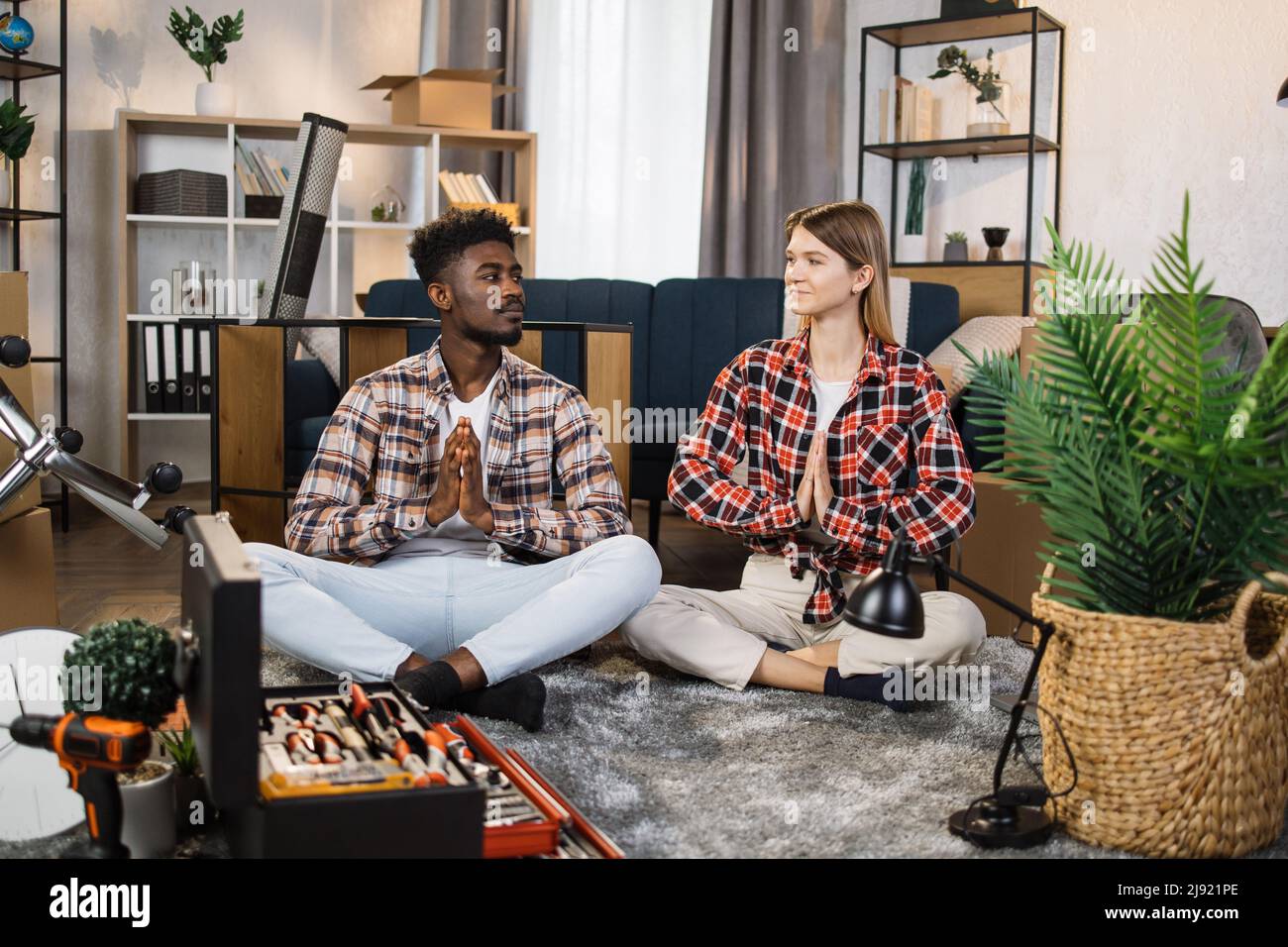 Multicultural young family sitting on floor and looking on each other while meditating together ...