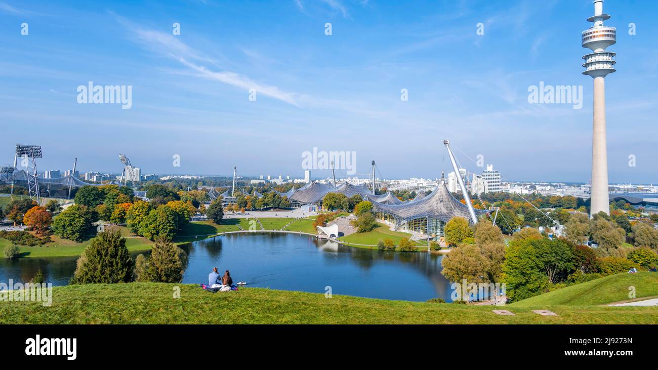 Two people sitting in the park with Olympic lake and Olympic tower ...