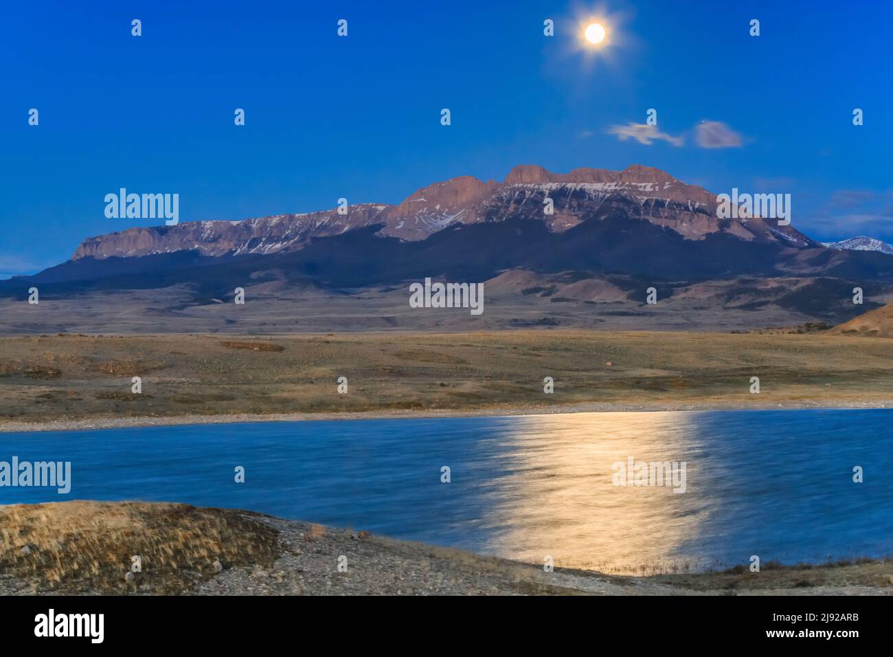 full moon setting behind sawtooth ridge and a prairie pond along the ...