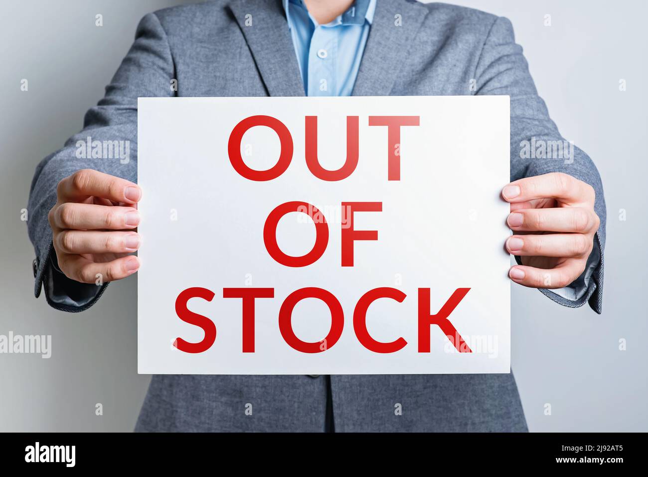 Unrecognizable man in grey suit holding a paper with text OUT OF STOCK ...
