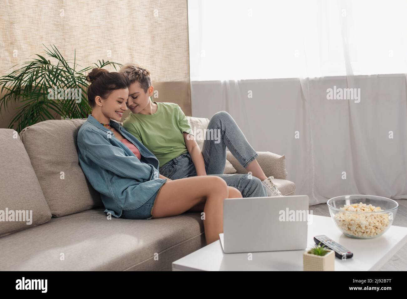 happy pansexual lovers sitting on couch near coffee table with laptop ...