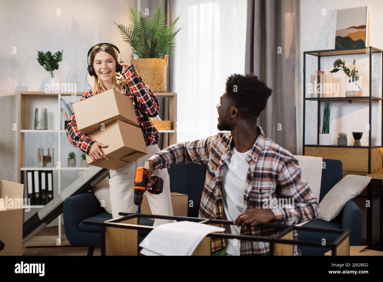Adorable young wife in headphones holding carton boxes and looking at ...