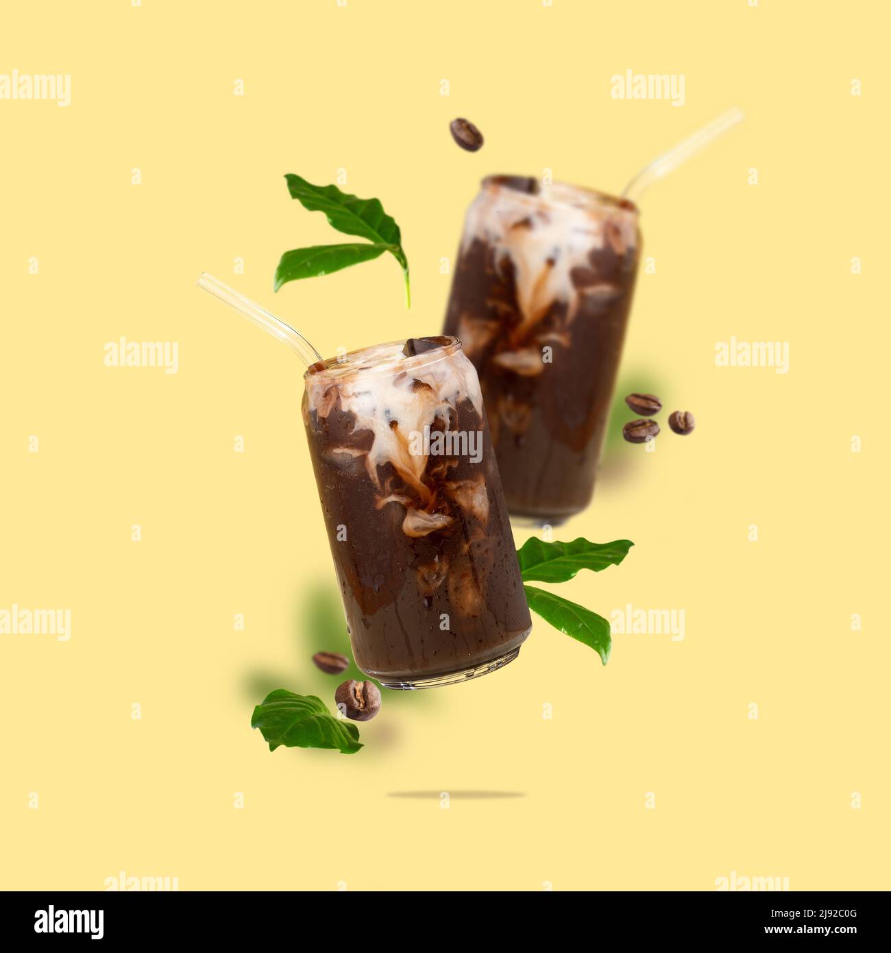 Two can-shaped glass with iced coffee, coffee beans and leaves in the ...