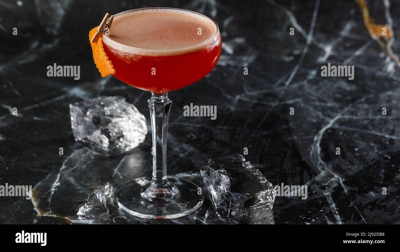 A red sour cocktail in a coupe glass garnished with an orange peel ...