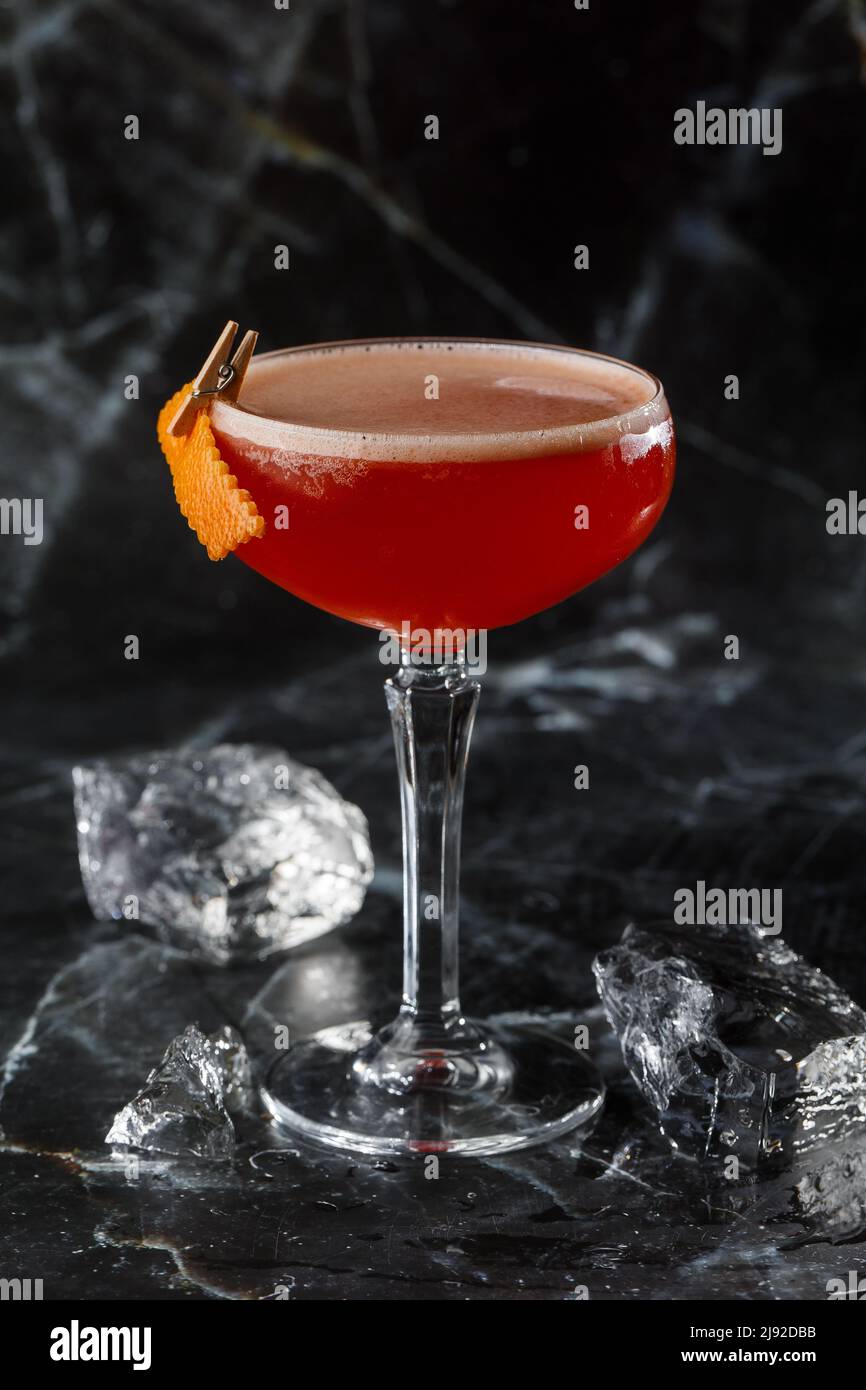 A red sour cocktail in a coupe glass garnished with an orange peel ...