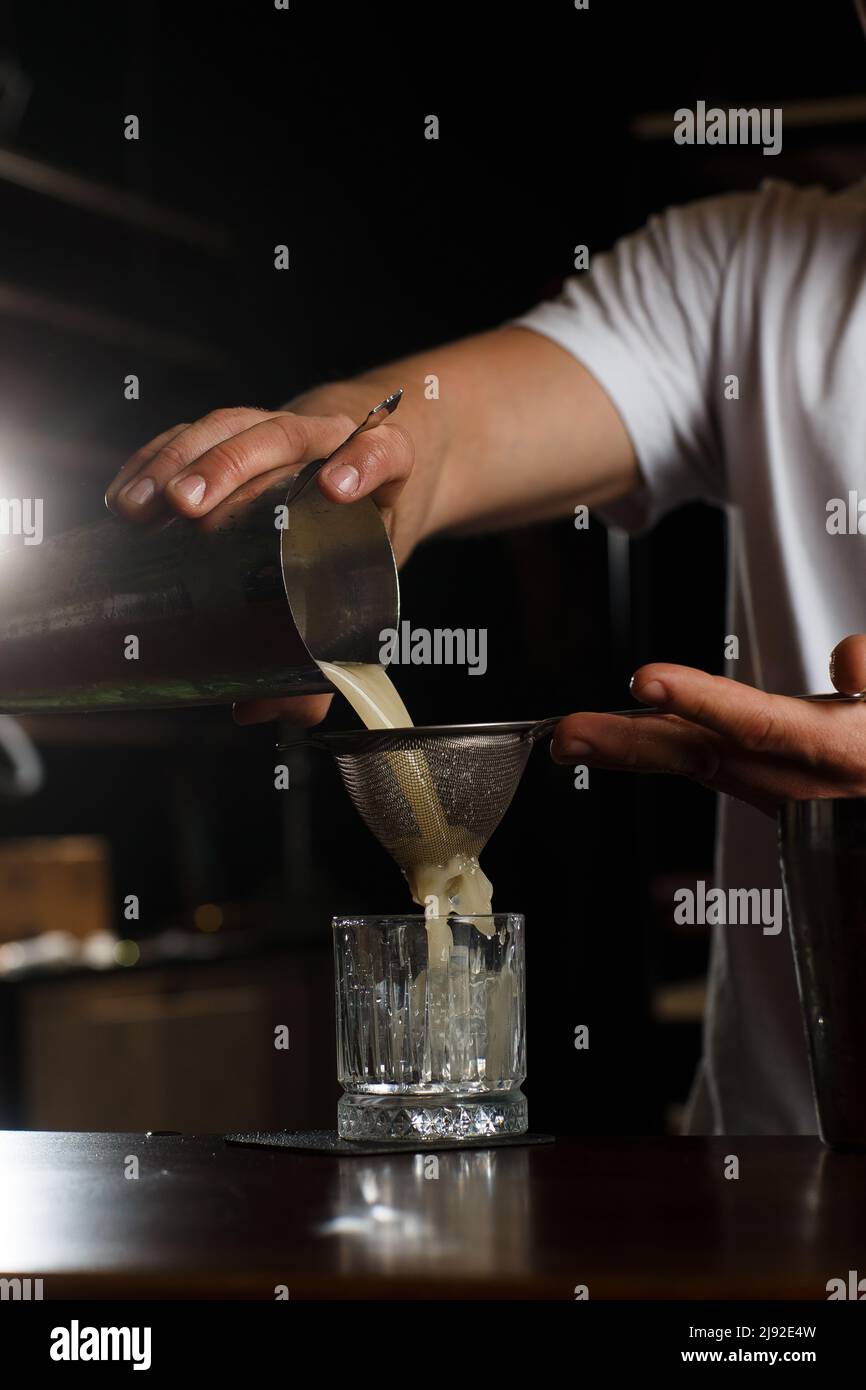man bartender carefully filters bright alcoholic cocktail from steel ...
