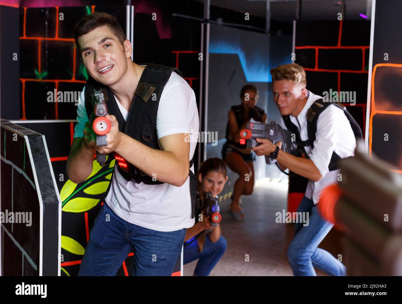 Smiling guys and girls in vests and with laser pistols playing laser ...