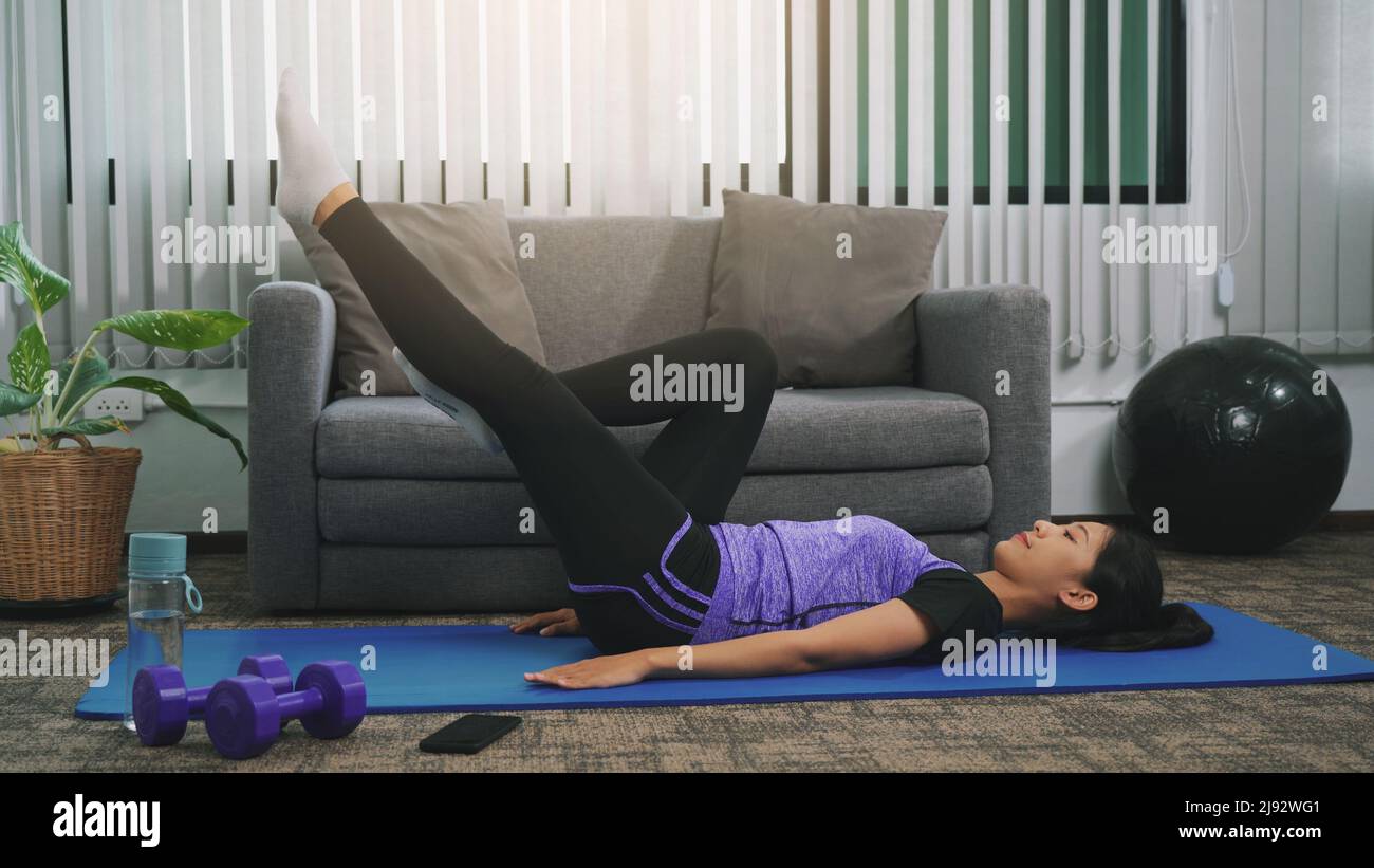 Asian woman practicing yoga at home while lying on a mat and stretching ...