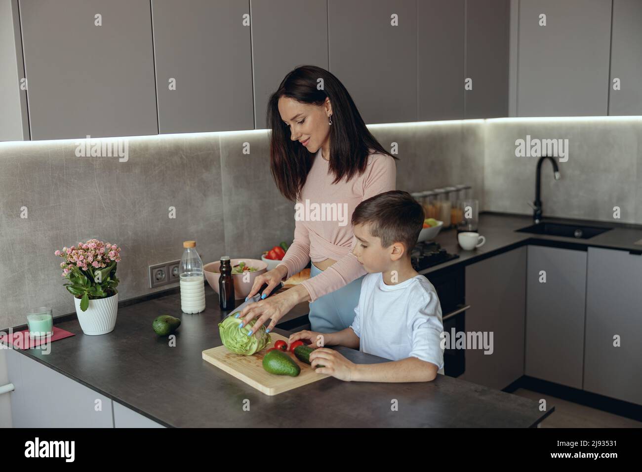 Young pretty mother cutting cabbage and preparing vegetables in kitchen ...