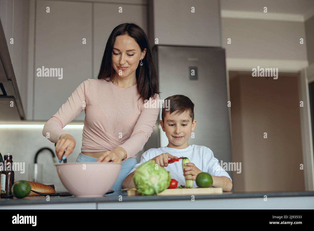 Portrait shot of beautiful mother cooking and cute son helping to peel ...