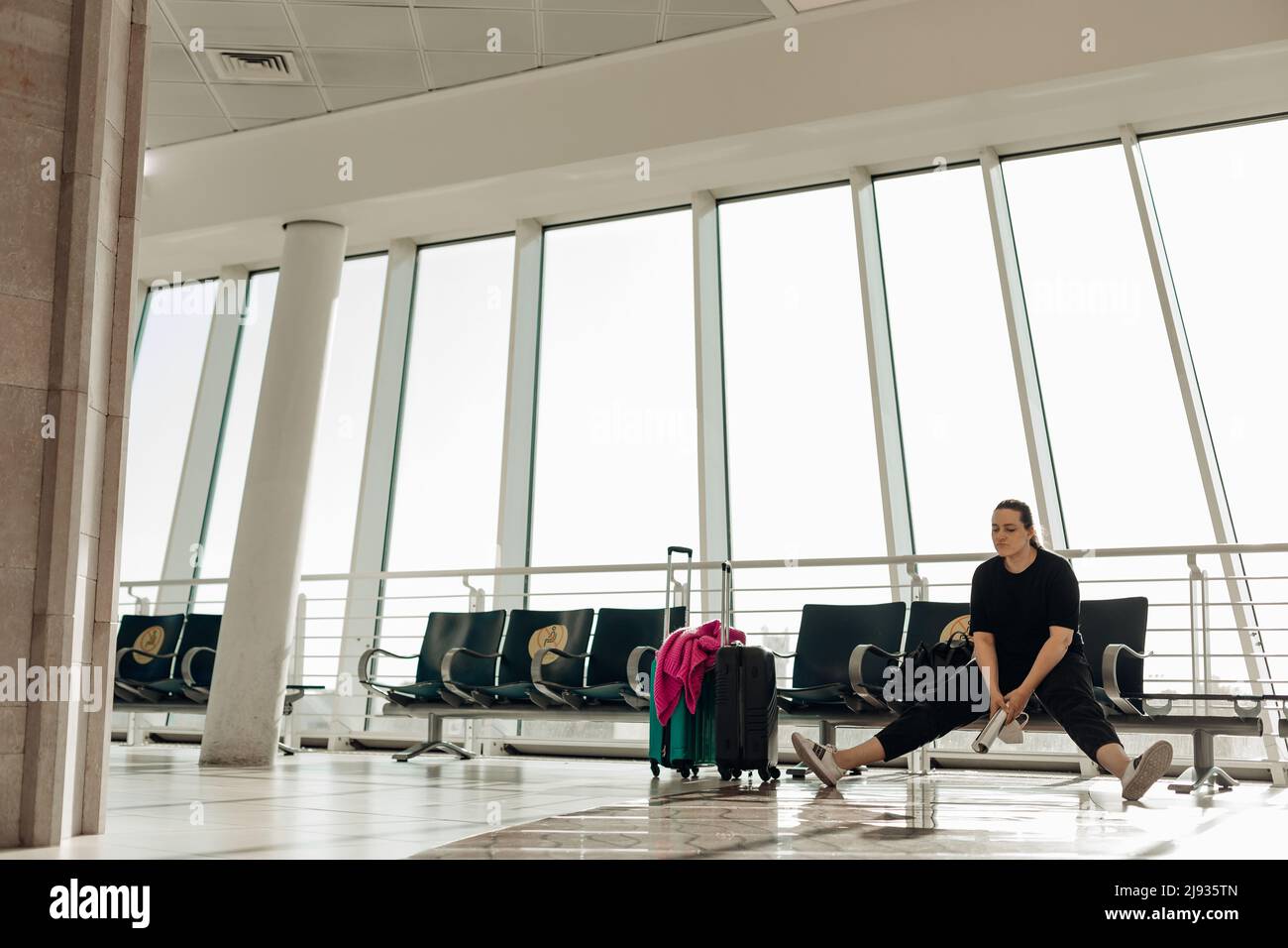 Woman passenger wearing black clothes, sitting on chair seat in transit ...