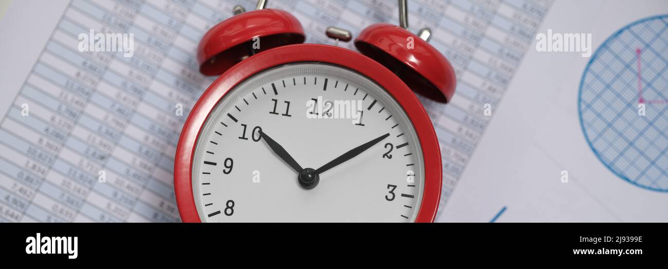 Red alarm clock lying on documents with graphs and numbers closeup ...