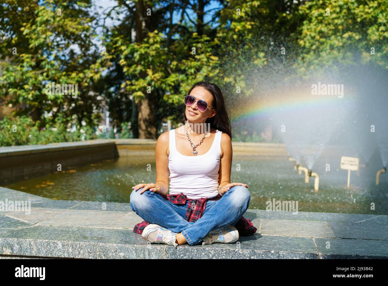 Beautiful happy woman sitting near fountain. Girl in casual clothes in ...