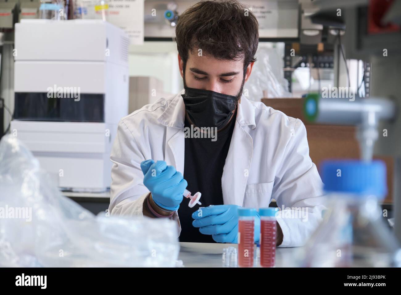 Scientist in white lab coat and face mask filter sample into HPLC vial ...