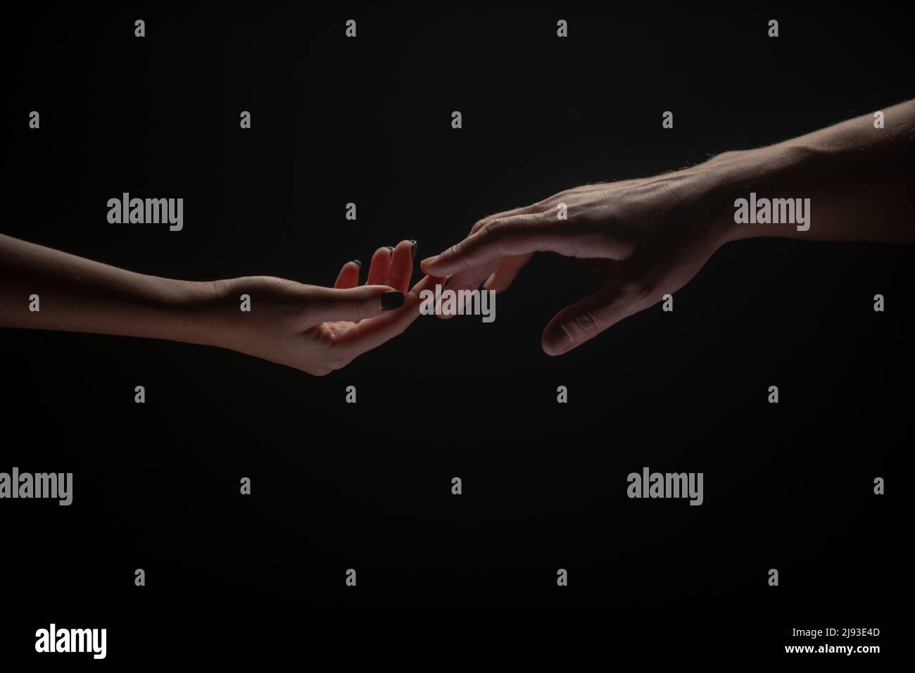 Romantic touch with fingers, love. Two hands stretch each other, black background. Couple in ...