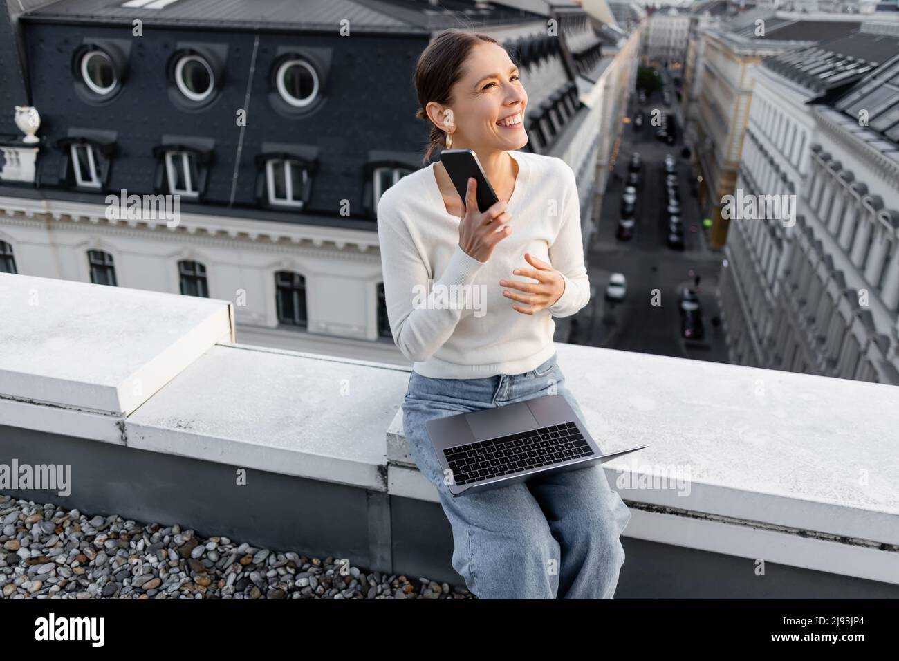 excited woman laughing during conversation on smartphone near laptop on ...