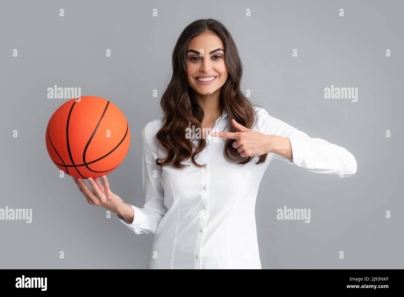 Happy woman pointing finger on basketball ball, isolated on gray ...