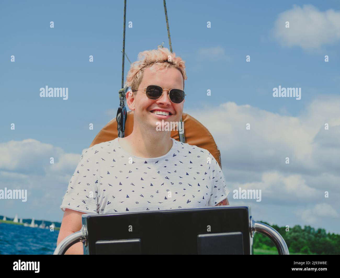 smiling candid blond hair young man steering wheel on sailboat or yacht ...