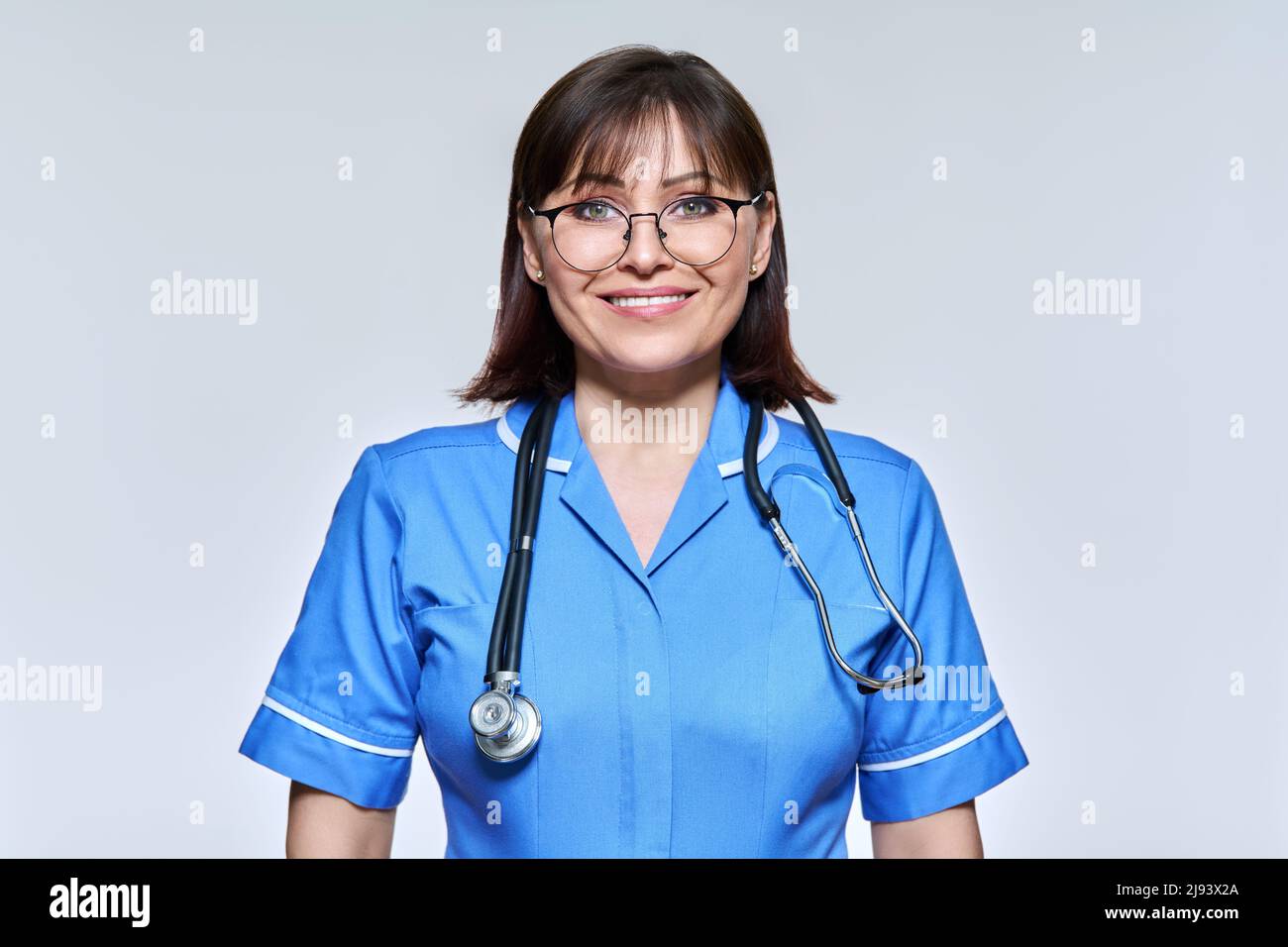 Headshot portrait of nurse in blue uniform looking at camera on light ...