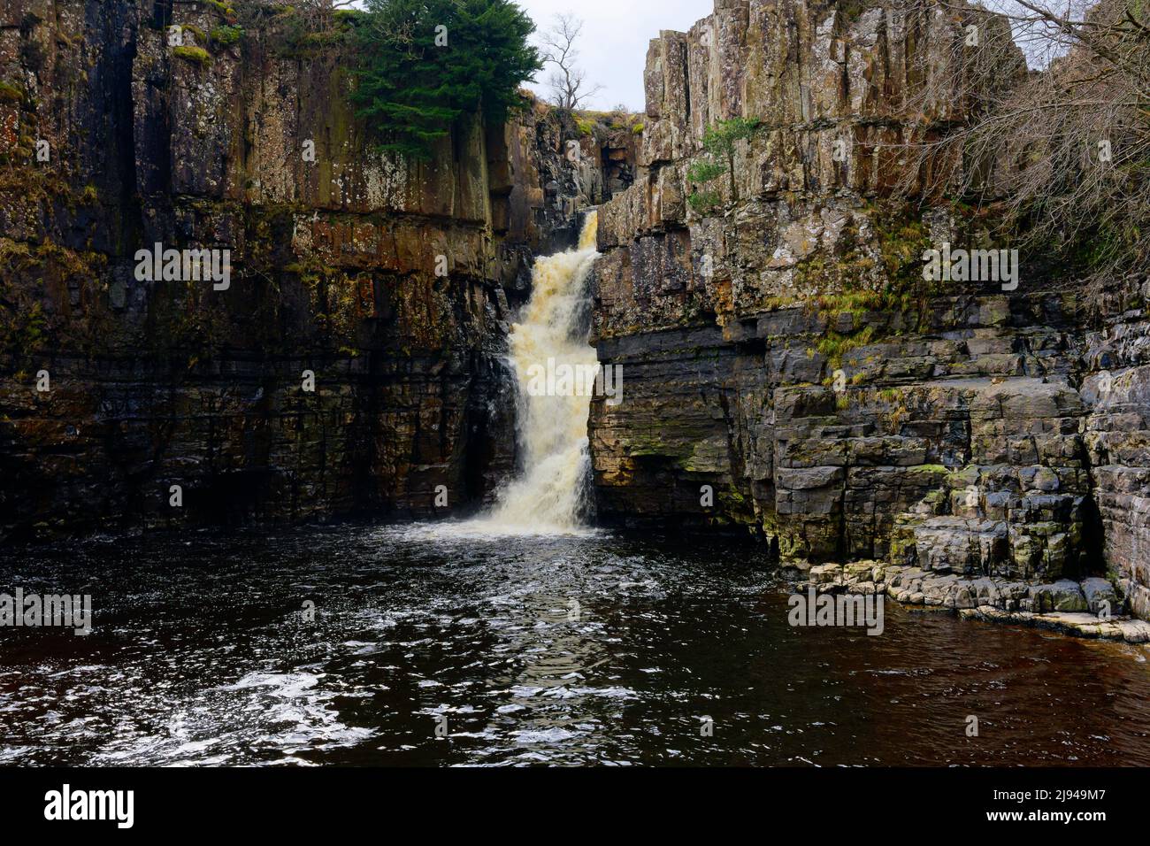 The River Tees drops over High Force waterfall to a shallow pool below ...