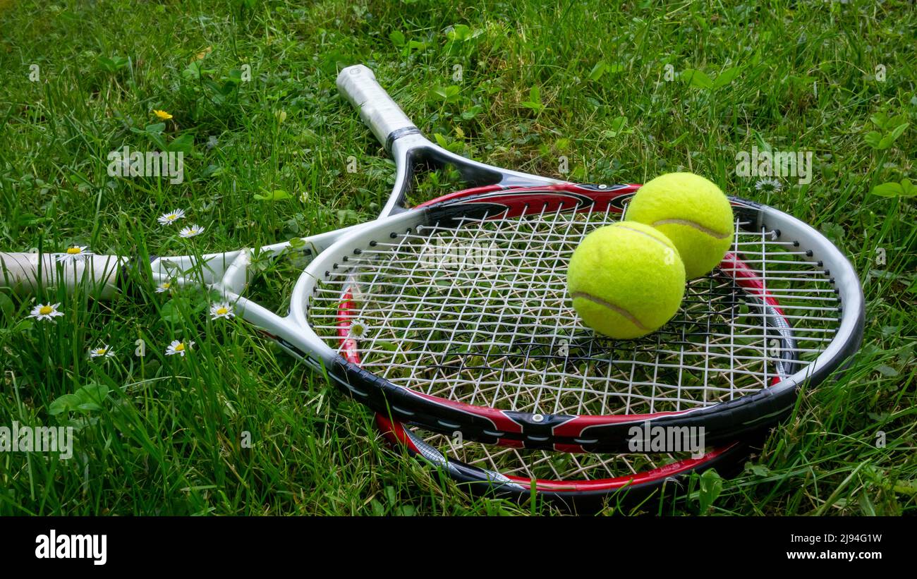 Two tennis rackets and two yellow balls against summery green meadow ...