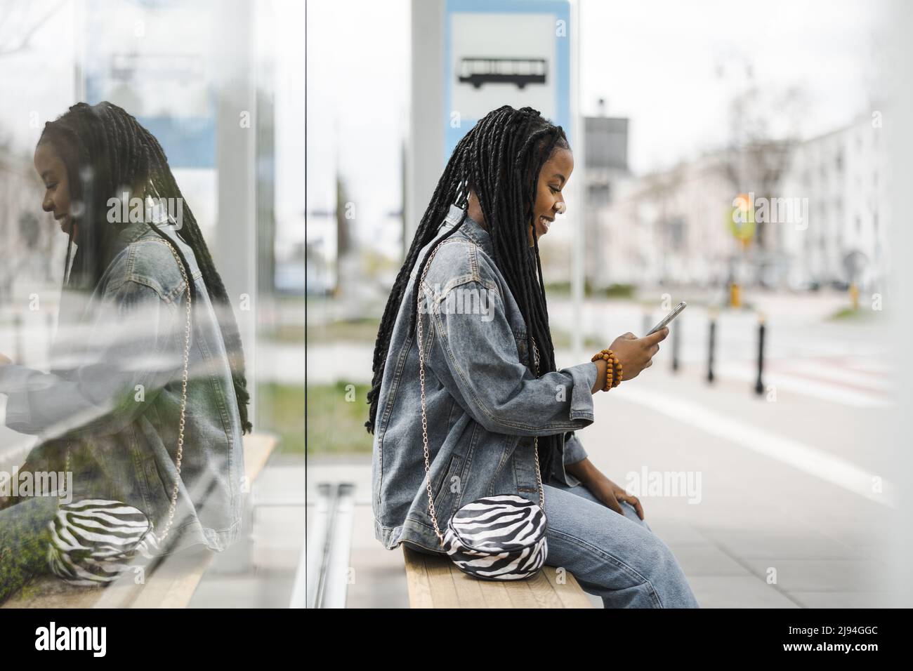 Young woman waiting for a bus at a bus stop Stock Photo - Alamy
