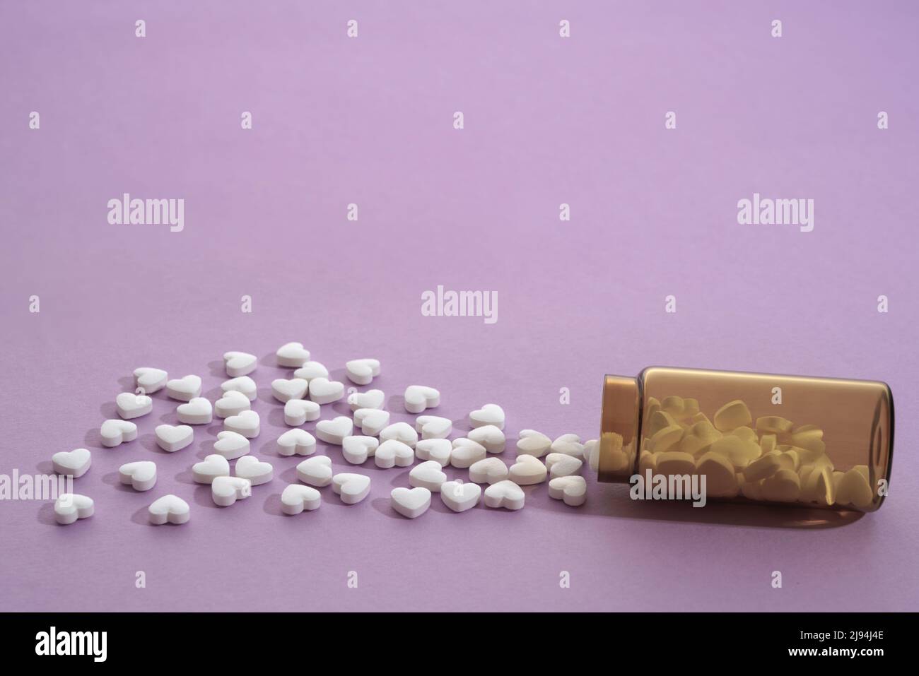 Spilled heart shaped pills bottle on purple background with copy space ...